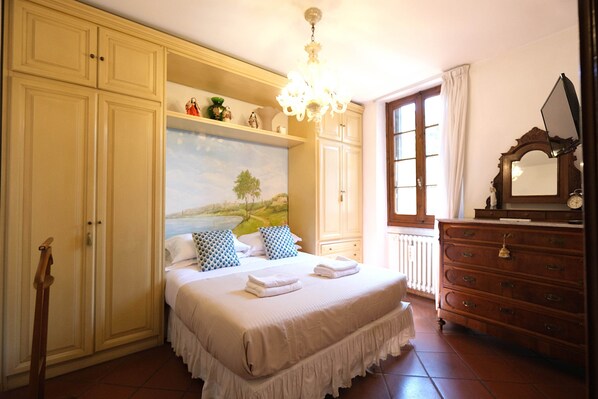 Quarto com cama, penteadeira, pintura e lustre.