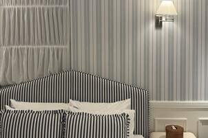 Quarto de hotel com papel de parede listrado, cama com roupa de cama listrada, luminária de cabeceira e caixa de lenços.