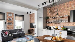 A modern kitchen with a brick wall, white cabinets, and a dining area with a wooden table and chairs.