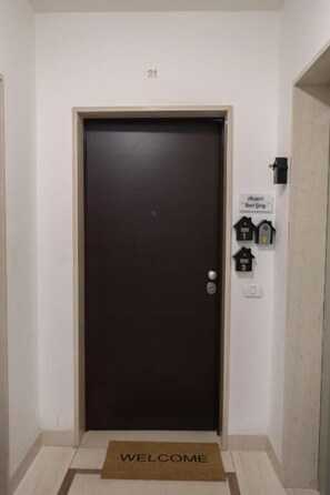Uma porta marrom escura com um tapete de boas-vindas na entrada. Uma placa acima da porta indica o número do quarto 21.