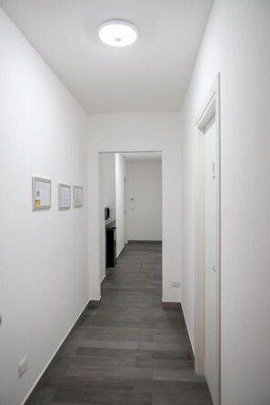 Um corredor estreito com piso de madeira, paredes brancas e uma porta no final.