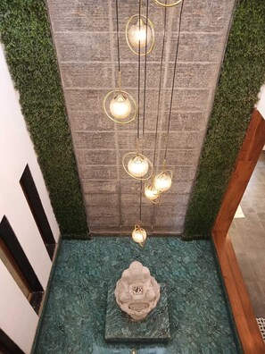 Uma escadaria com uma parede verde texturizada, uma escultura decorativa de flores na base e uma série de luminárias pendentes.