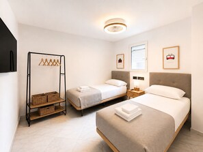Quarto de hotel com duas camas, um guarda-roupa, uma televisão e uma luminária no teto.