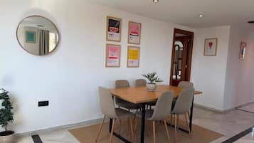 Uma sala de jantar com uma mesa de madeira e seis cadeiras, uma planta em vaso e um espelho na parede.