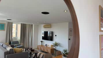 Uma sala de estar moderna com um sofá, uma mesa de centro, uma TV na parede e piso quadriculado.