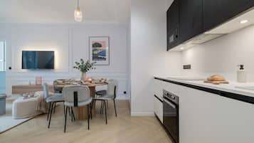 Uma cozinha moderna com armários brancos, uma sala de jantar com mesa e cadeiras de madeira, e uma televisão de tela plana na parede.