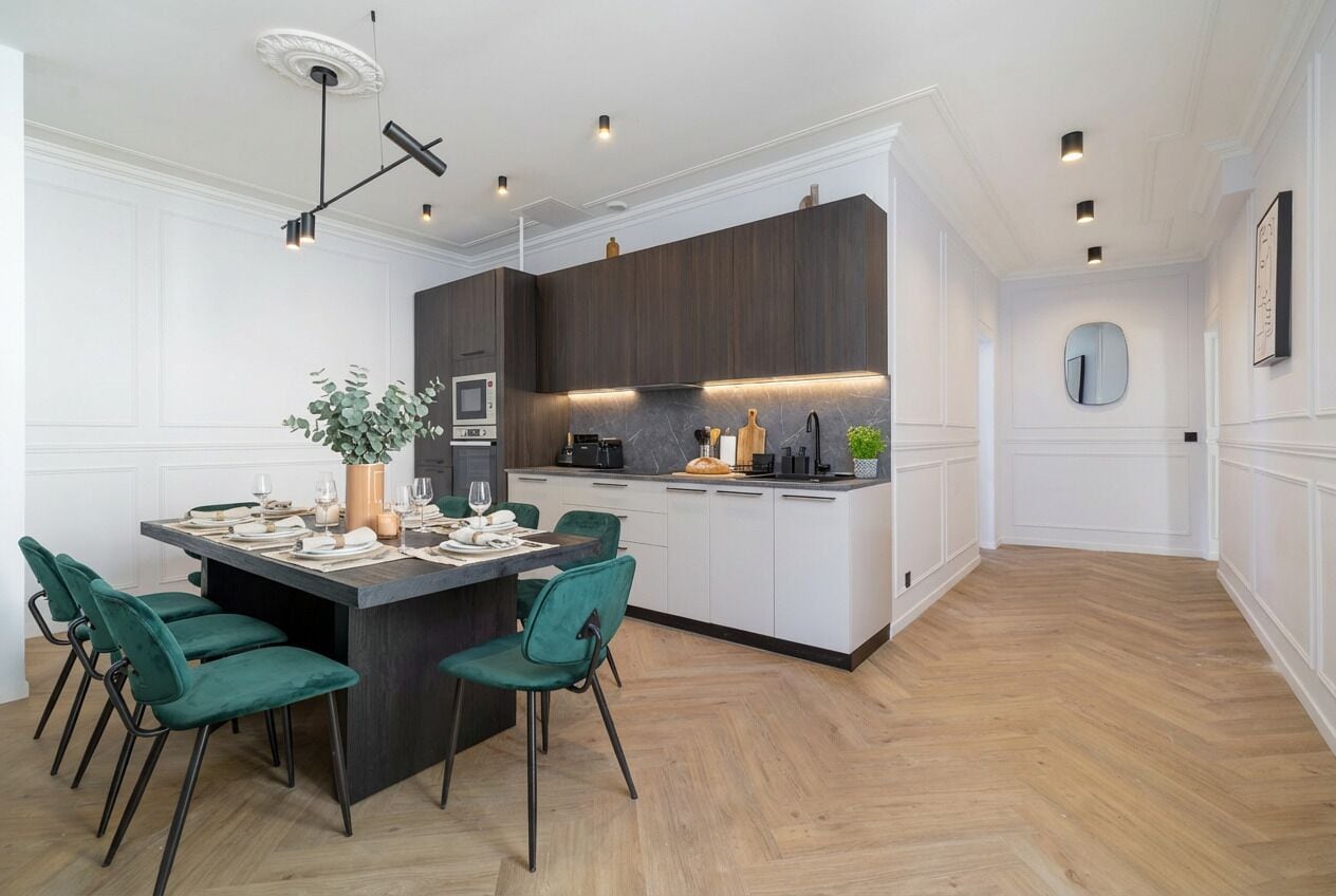 Uma cozinha moderna com armários escuros, uma ilha central e uma área de refeições com cadeiras verdes.