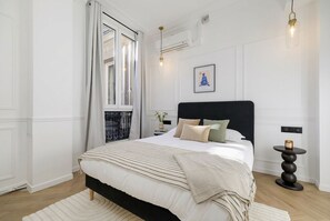 Um quarto com uma cama grande, uma mesa de cabeceira com uma vela e uma janela com cortinas.