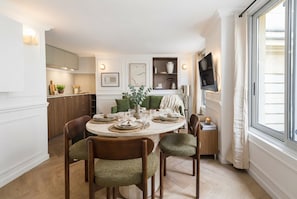 Uma sala de jantar com uma mesa redonda posta para quatro pessoas, cercada por cadeiras de madeira com estofamento verde.