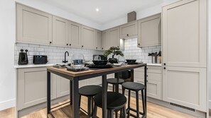 Uma cozinha moderna com armários brancos, uma mesa de madeira e banquetas pretas.