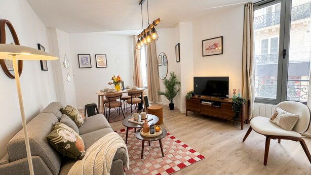 Uma sala de estar com sofá, mesa de jantar, televisão e uma janela grande.