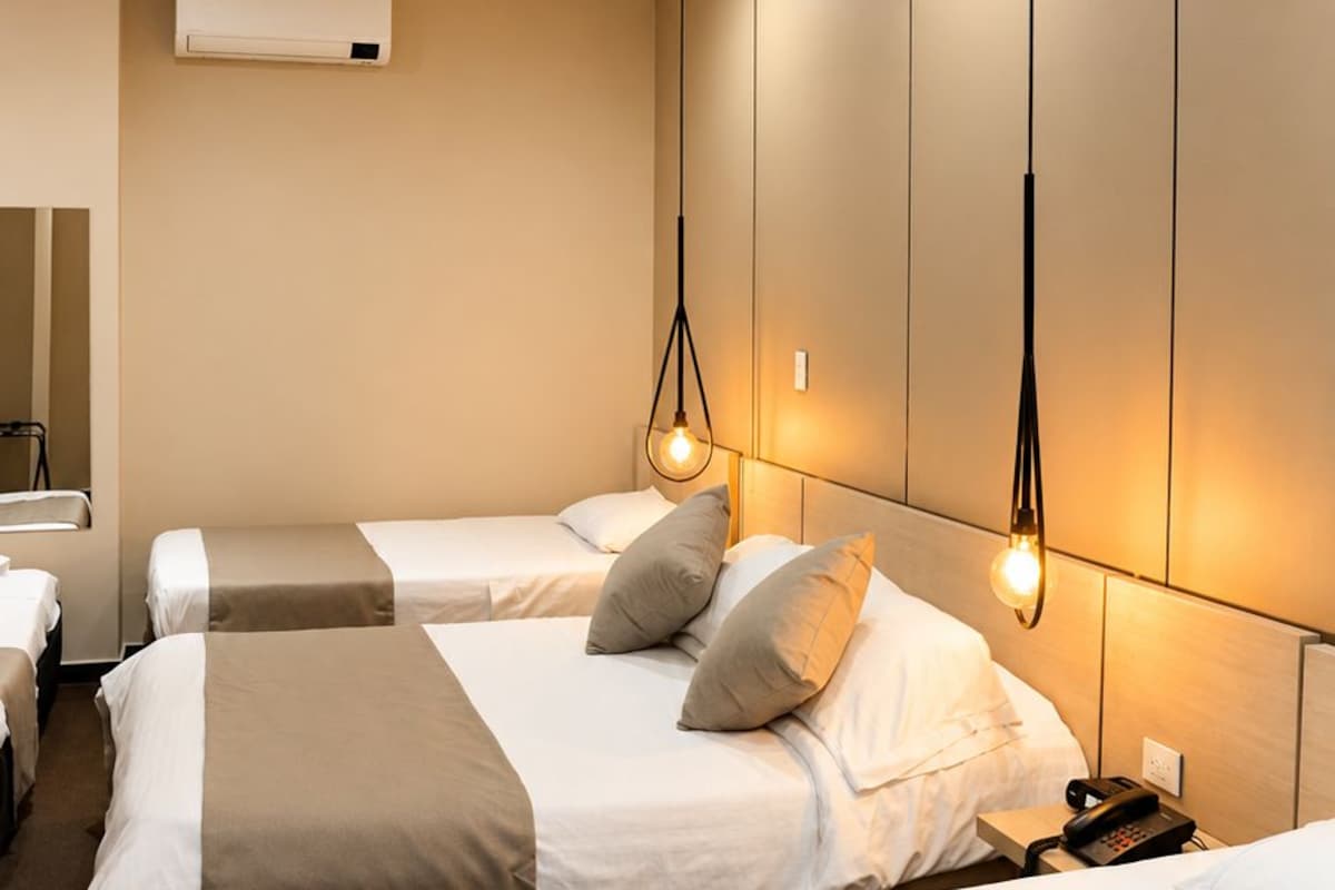 Quarto de hotel com três camas, ar condicionado e luminárias pendentes.