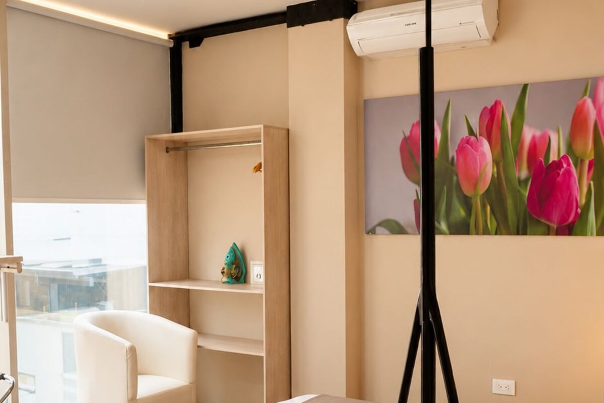 Quarto de hotel com cama, escrivaninha, cadeira, pintura de tulipas e luminária pendente.