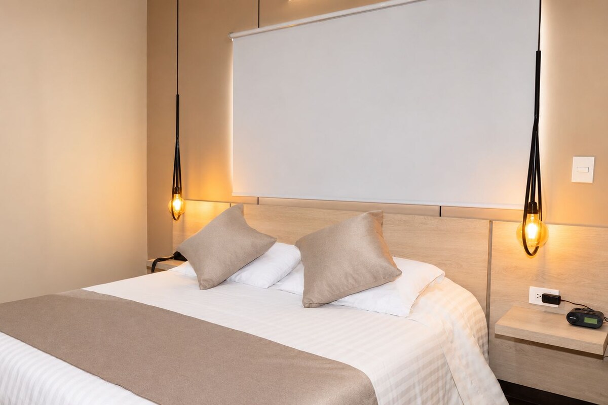 Quarto de hotel com uma cama grande, mesas de cabeceira, um espelho e luminárias na parede.