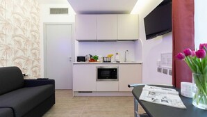 Um espaço compacto com cozinha compacta, um sofá, uma mesa de jantar com um jornal e um vaso com flores.