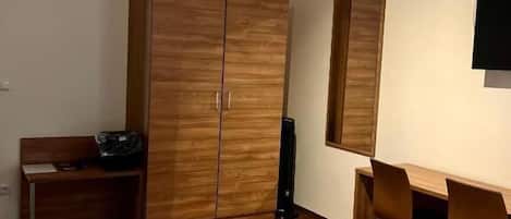 Quarto de hotel com cama, escrivaninha, cadeira, guarda-roupa e televisão.