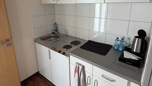 Uma cozinha compacta com armários brancos, pia de aço inoxidável, fogão a gás e cafeteira.