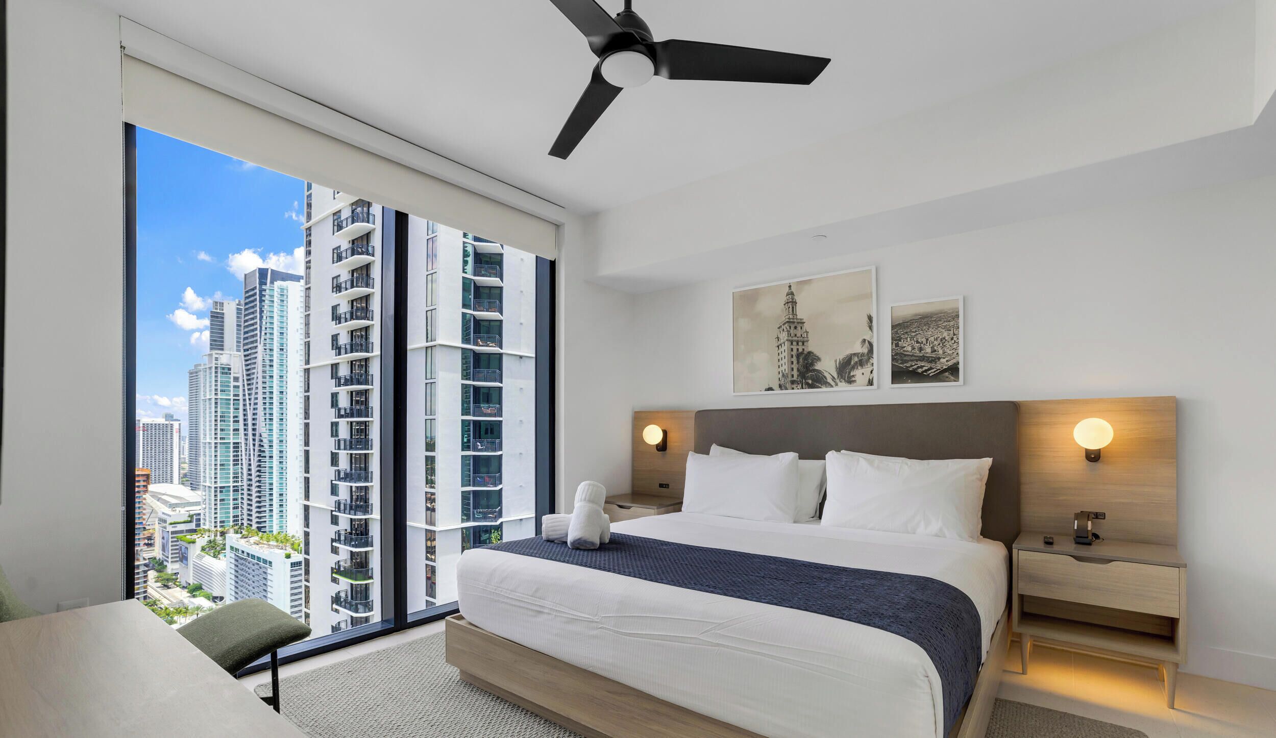 Quarto de hotel moderno com uma cama grande, ventilador de teto e vista para a cidade.