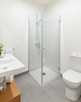 Casa de banho moderna com chuveiro em cabine de vidro, lavatório branco e sanita.