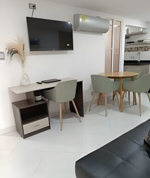 Uma sala de estar moderna com uma televisão de tela plana na parede, uma área de jantar com uma mesa redonda e cadeiras, e um sofá.