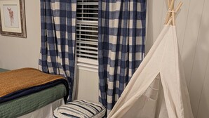 Um quarto aconchegante com uma cama, uma pequena tenda branca e uma janela com cortinas xadrez.