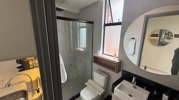 Uma casa de banho moderna com cabine de chuveiro em vidro, sanita, lavatório e espelho.