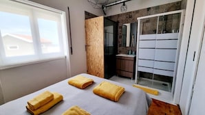 Quarto com cama, janela, porta de madeira, banheiro com espelho e armário com porta deslizante.