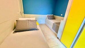 Quarto pequeno e compacto com duas camas, um sofá e uma parede amarelo vivo.