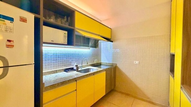 Uma cozinha compacta com armários amarelos, micro-ondas embutido e pia de aço inoxidável.