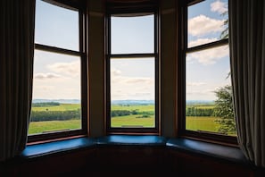 Quarto de canto com janela saliente com vista para uma paisagem verde.