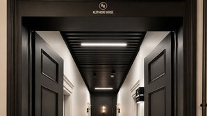 Um corredor com portas pretas, uma placa com a inscrição 'KLEPARSKI HOUSE' e um luminária no teto.