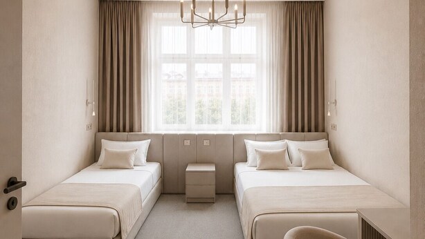 Quarto de hotel com duas camas, uma pequena mesa, uma cadeira e uma janela com cortinas.