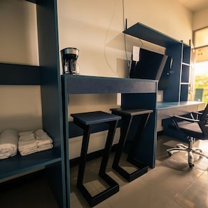 Um espaço de escritório moderno, com uma mesa, duas cadeiras, uma máquina de café e uma estante com toalhas dobradas.