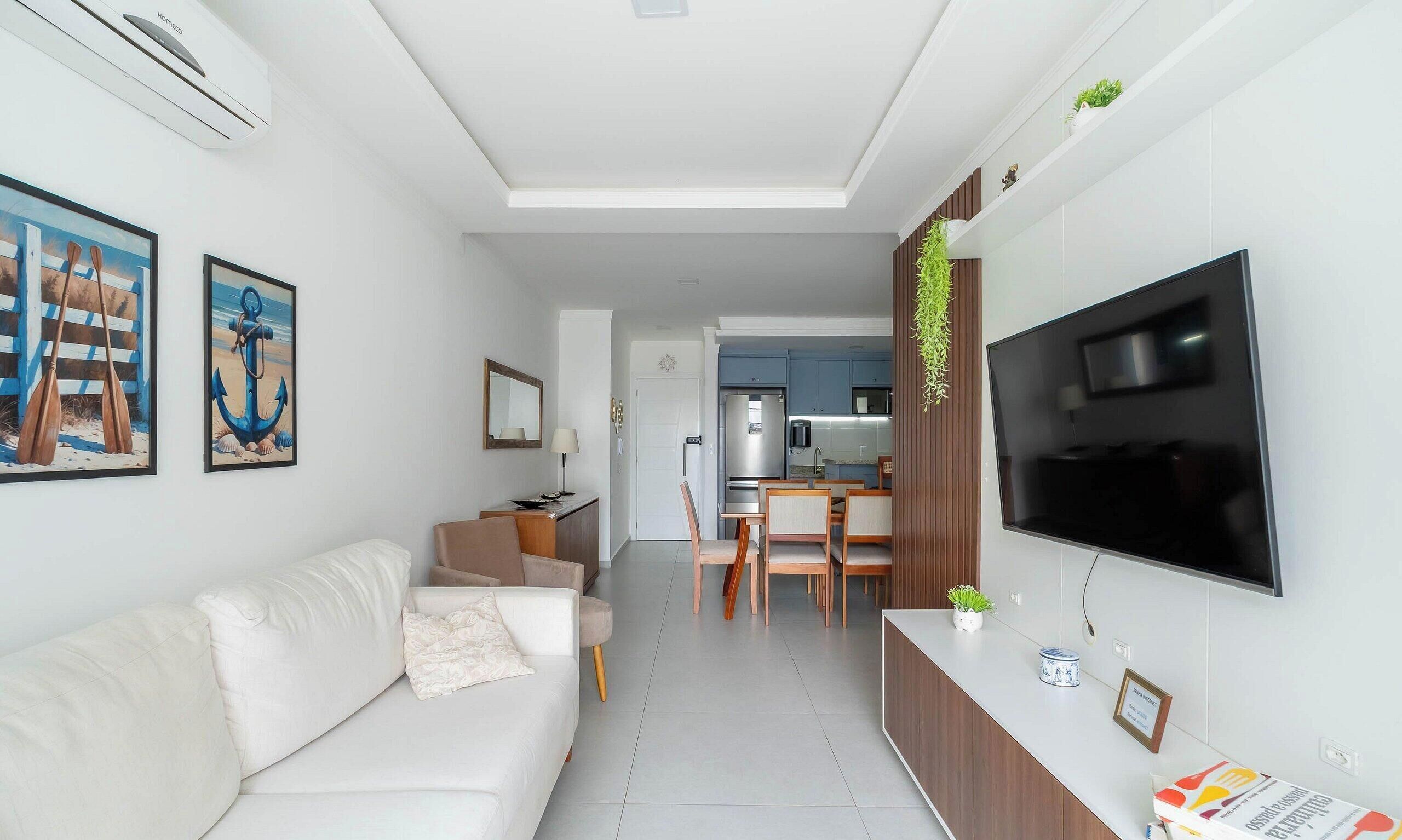 Uma sala de estar moderna com um sofá branco, uma televisão de tela plana e obras de arte nas paredes.