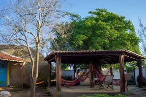 Uma área externa rústica com um gazebo de madeira, uma rede e uma cadeira rede.
