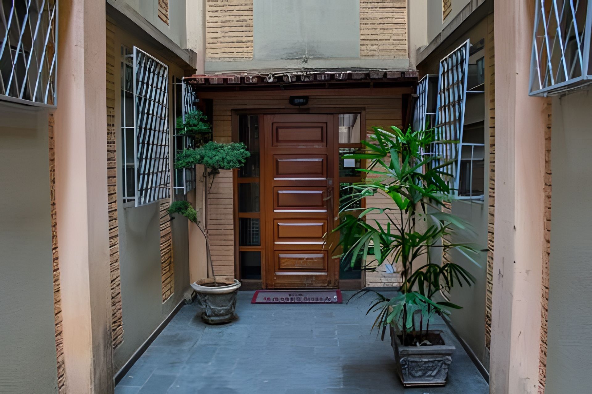 Um pátio estreito com porta de madeira, plantas em vasos e chão de azulejos.