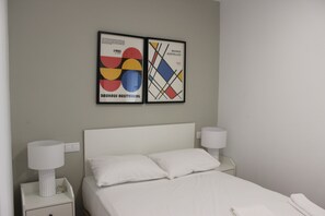 Quarto de hotel com uma cama, duas luminárias de cabeceira e duas obras de arte abstrata emolduradas na parede.
