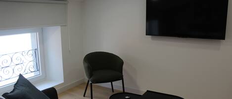 Uma sala de estar moderna com televisão de tela plana na parede, uma poltrona verde-escuro, uma mesa de centro preta e um sofá com almofada preta.
