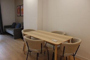 Um quarto com uma mesa de madeira e quatro cadeiras, um sofá cinzento e uma luminária.