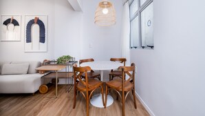 Uma área de refeições moderna com uma mesa redonda e cadeiras de madeira, um lustre e uma parede branca com quadros.