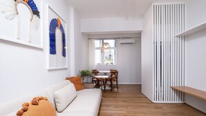 Uma sala de estar moderna com um sofá branco, uma mesa de jantar de madeira e um painel branco com ripas verticais.