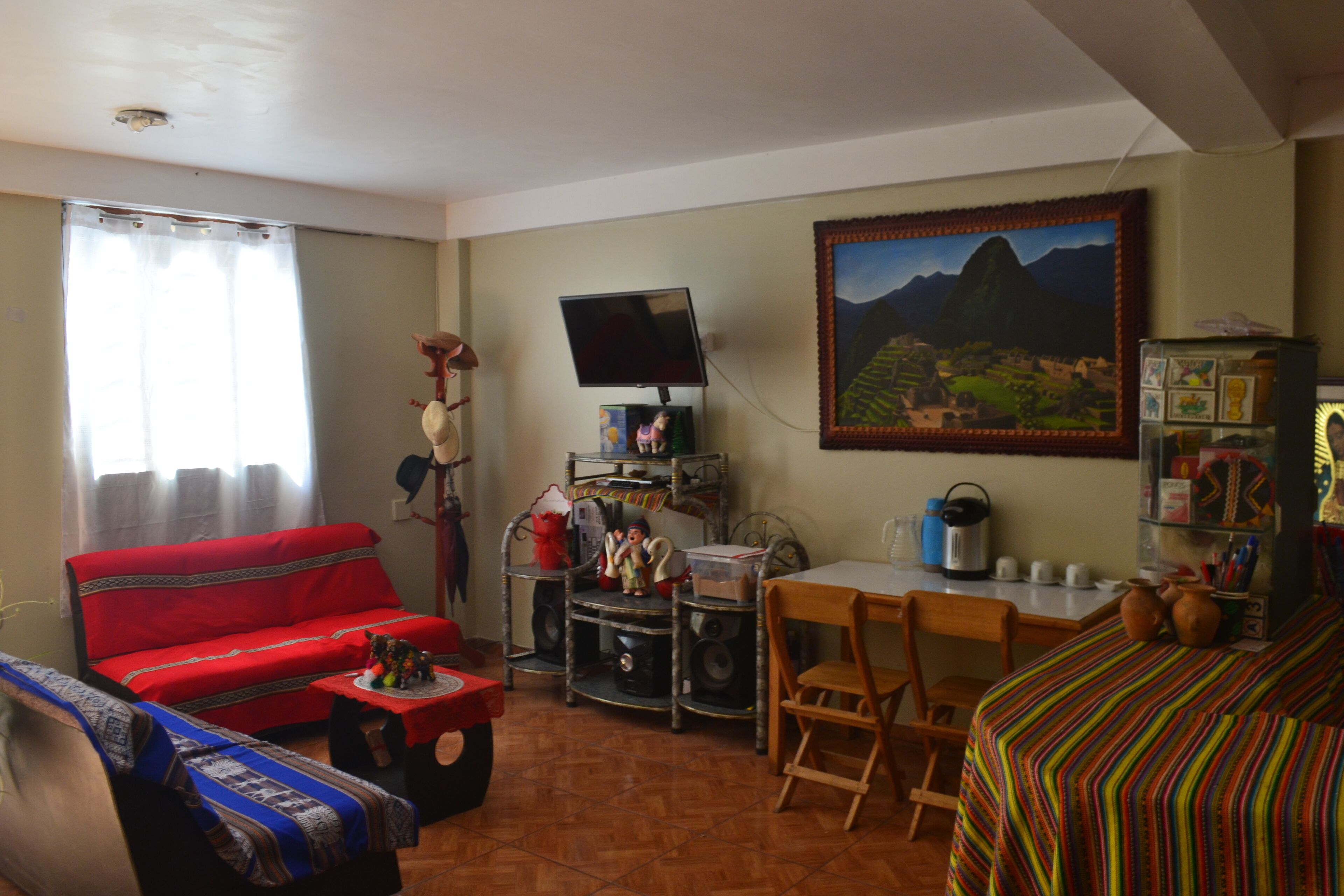 Uma sala de estar com um sofá vermelho, uma televisão, uma mesa de jantar com cadeiras e uma estante de livros.