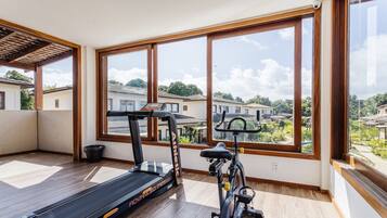 Varanda espaçosa com esteira e bicicleta ergométrica, grandes janelas com vista para uma área residencial.