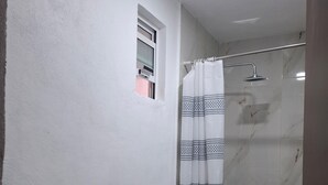 Casa de banho com sanita, lavatório, chuveiro e uma pequena janela.