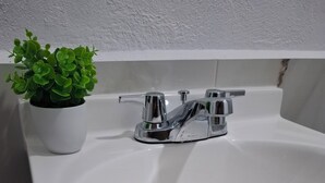 Uma pia de banheiro branca com uma torneira cromada e uma pequena planta em vaso.