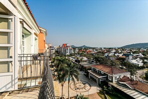 Área residencial com vista para uma montanha ao longe, pátio pavimentado com palmeiras e um edifício com telhado de telhas vermelhas.