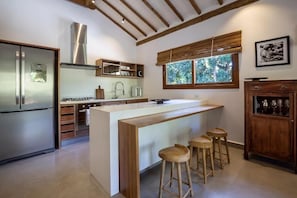 Uma cozinha moderna com uma ilha central, banquetas, geladeira de aço inoxidável e armário de madeira.