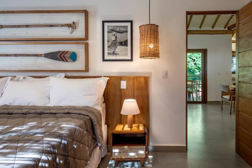 Quarto com uma cama grande, mesa de cabeceira com abajur, cabeceira de madeira e um quadro na parede.