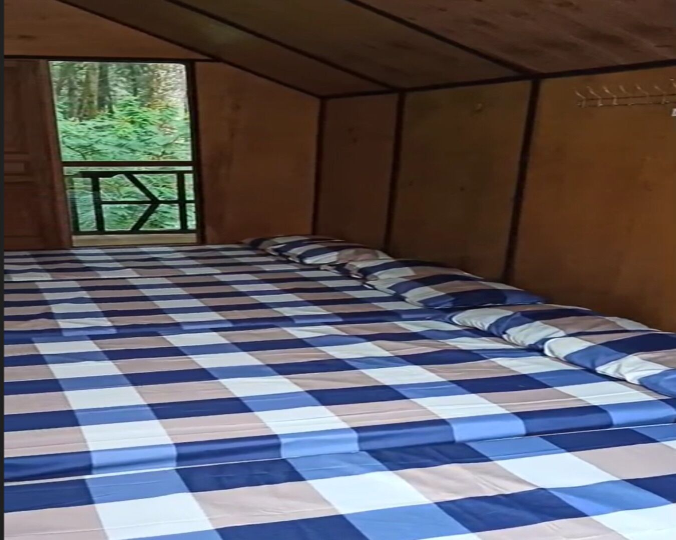 Quarto com colcha xadrez, paredes de madeira e varanda com vista para o verde.