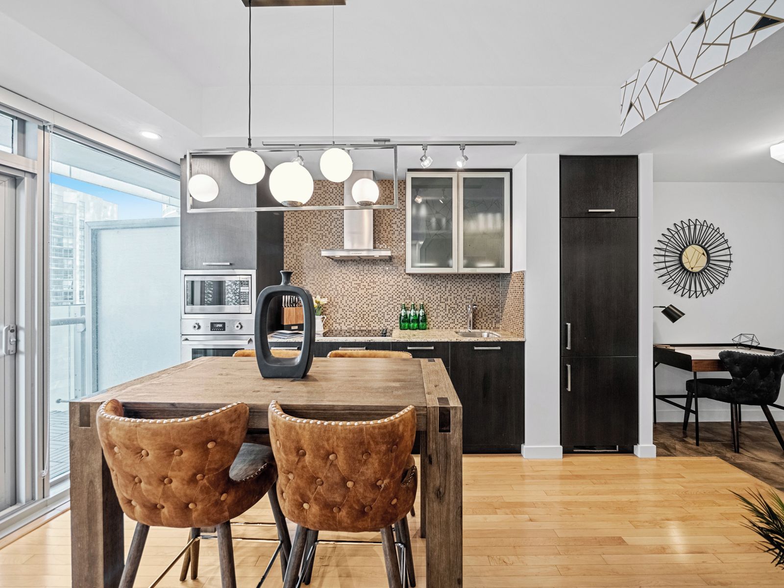 Cozinha moderna com área de refeições, apresentando uma mesa de madeira, duas cadeiras estofadas e iluminação pendente.